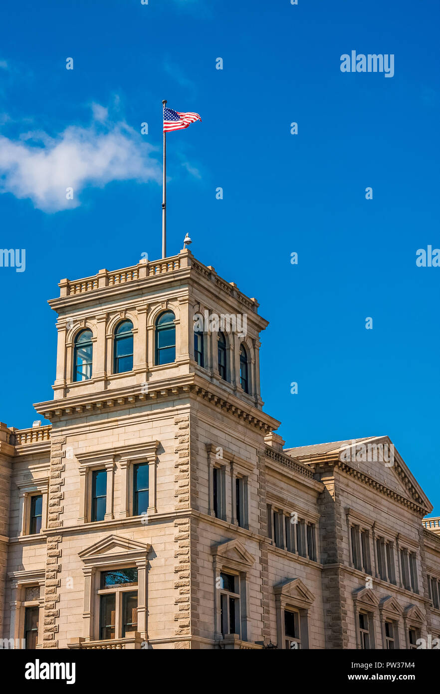 An old granite stone block building under blue skies with American flag ...