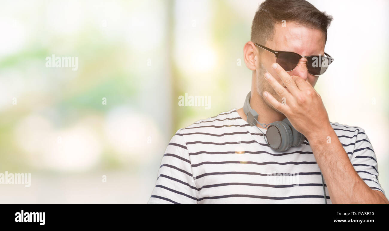 Handsome young man wearing headphones smelling something stinky and ...