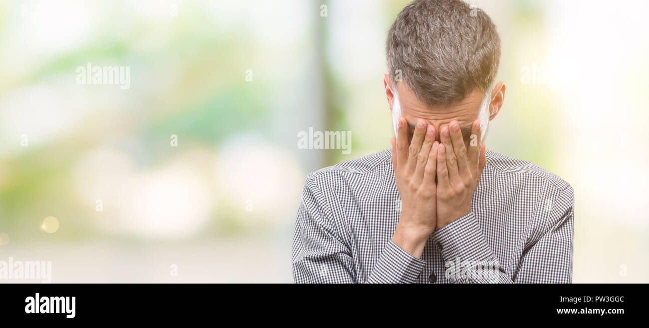 Young hipster man with sad expression covering face with hands while ...