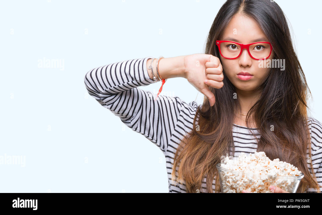 Young asian woman eating popcorn over isolated background with angry ...