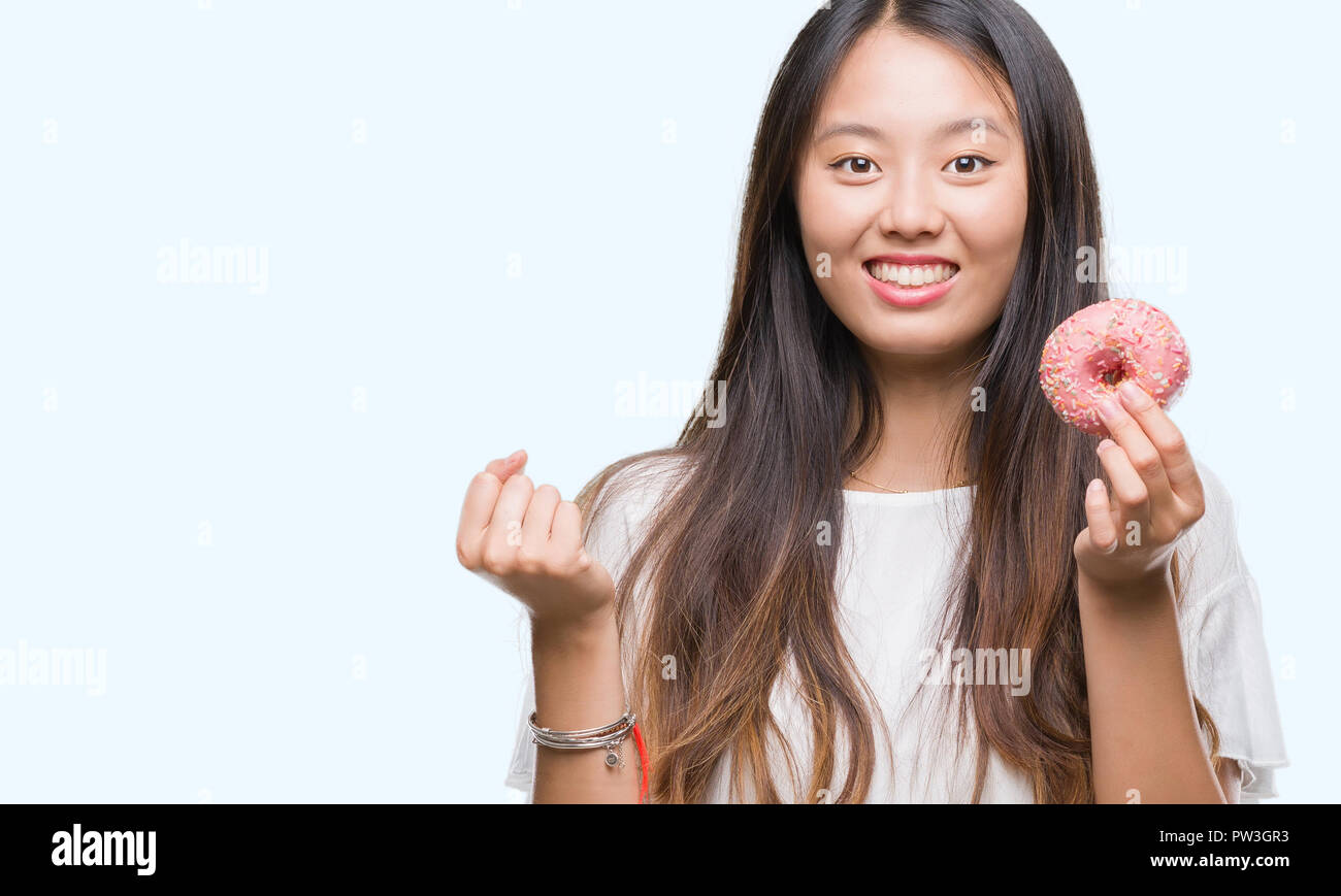 Young asian woman eating donut over isolated background screaming proud ...