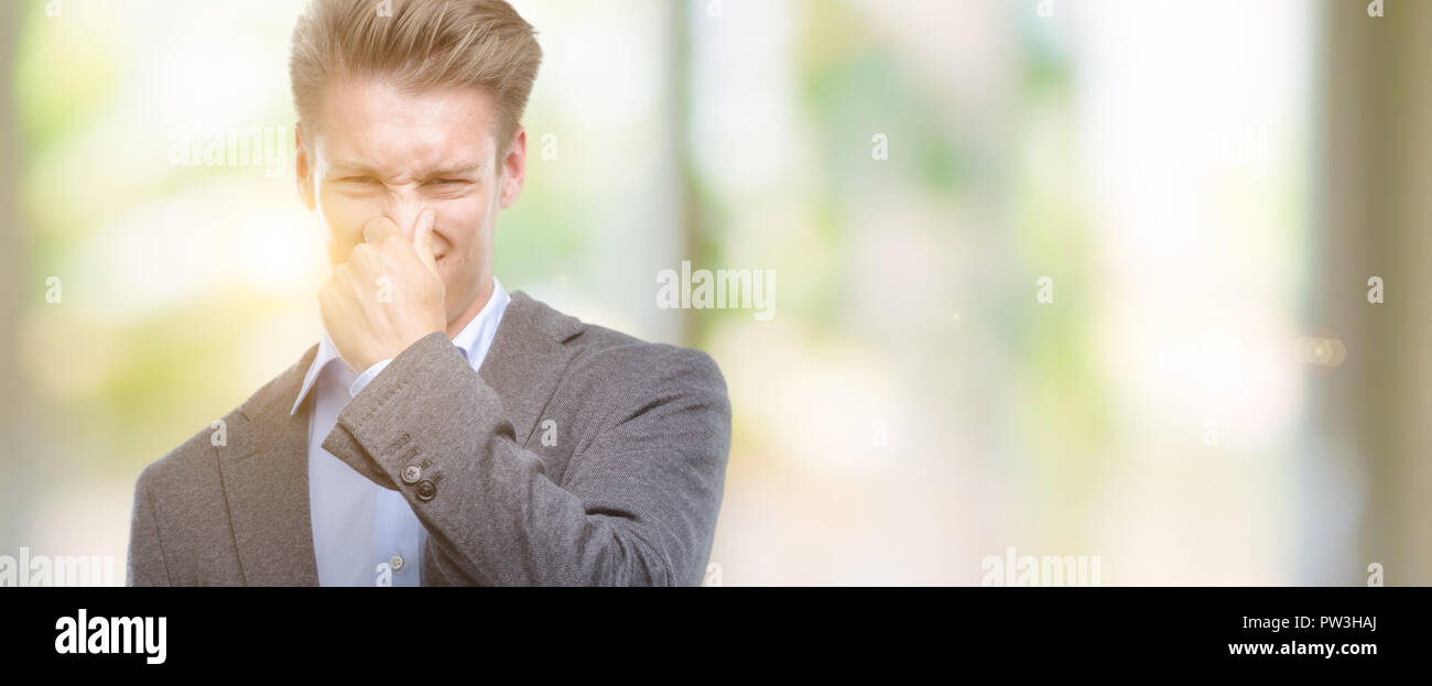 Young handsome blond business man smelling something stinky and ...
