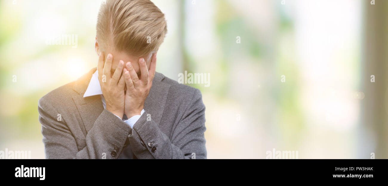 Young handsome blond business man with sad expression covering face ...