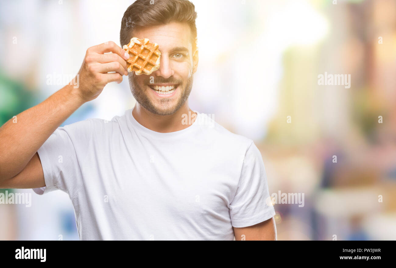 Young handsome man eating a sweet waffle over isolated background with ...