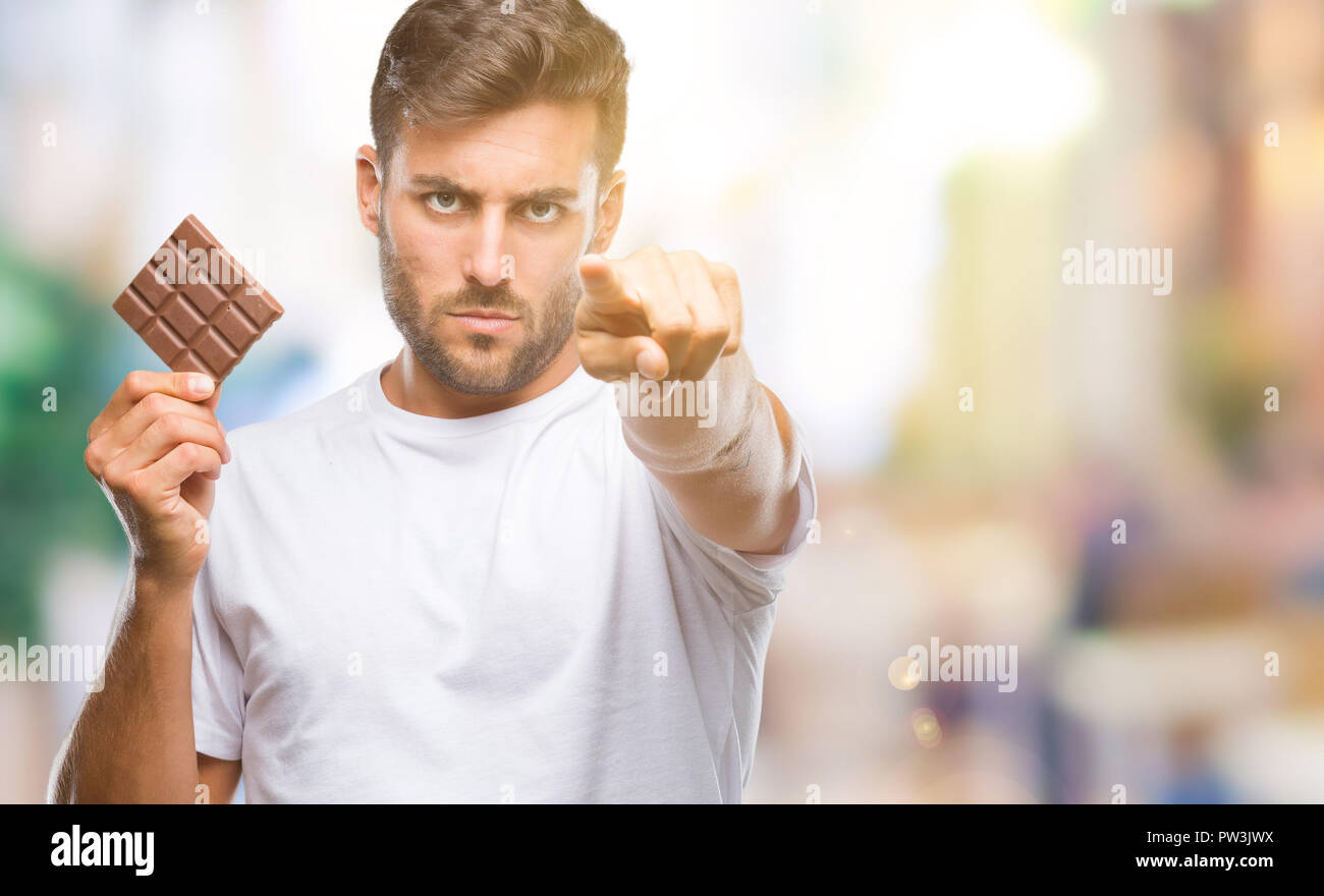 Young handsome man eating chocolate bar over isolated background ...