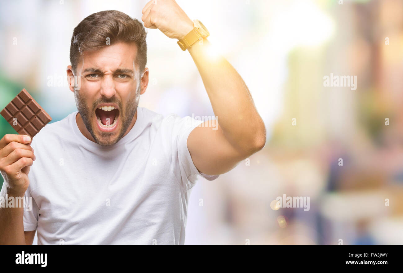 Young handsome man eating chocolate bar over isolated background ...