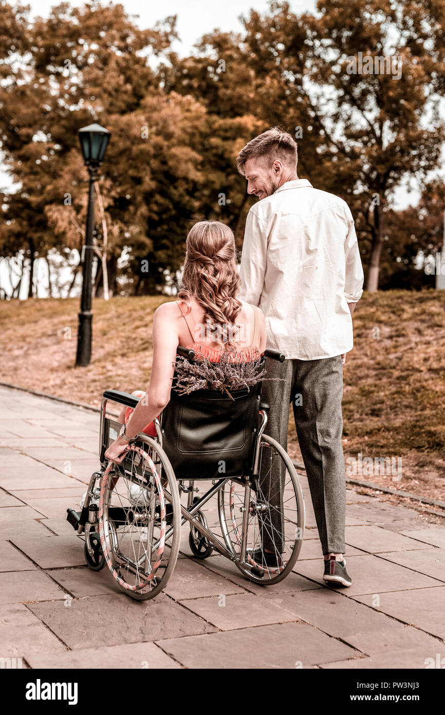 Happy man looking at his disabled girlfriend while walking with her ...
