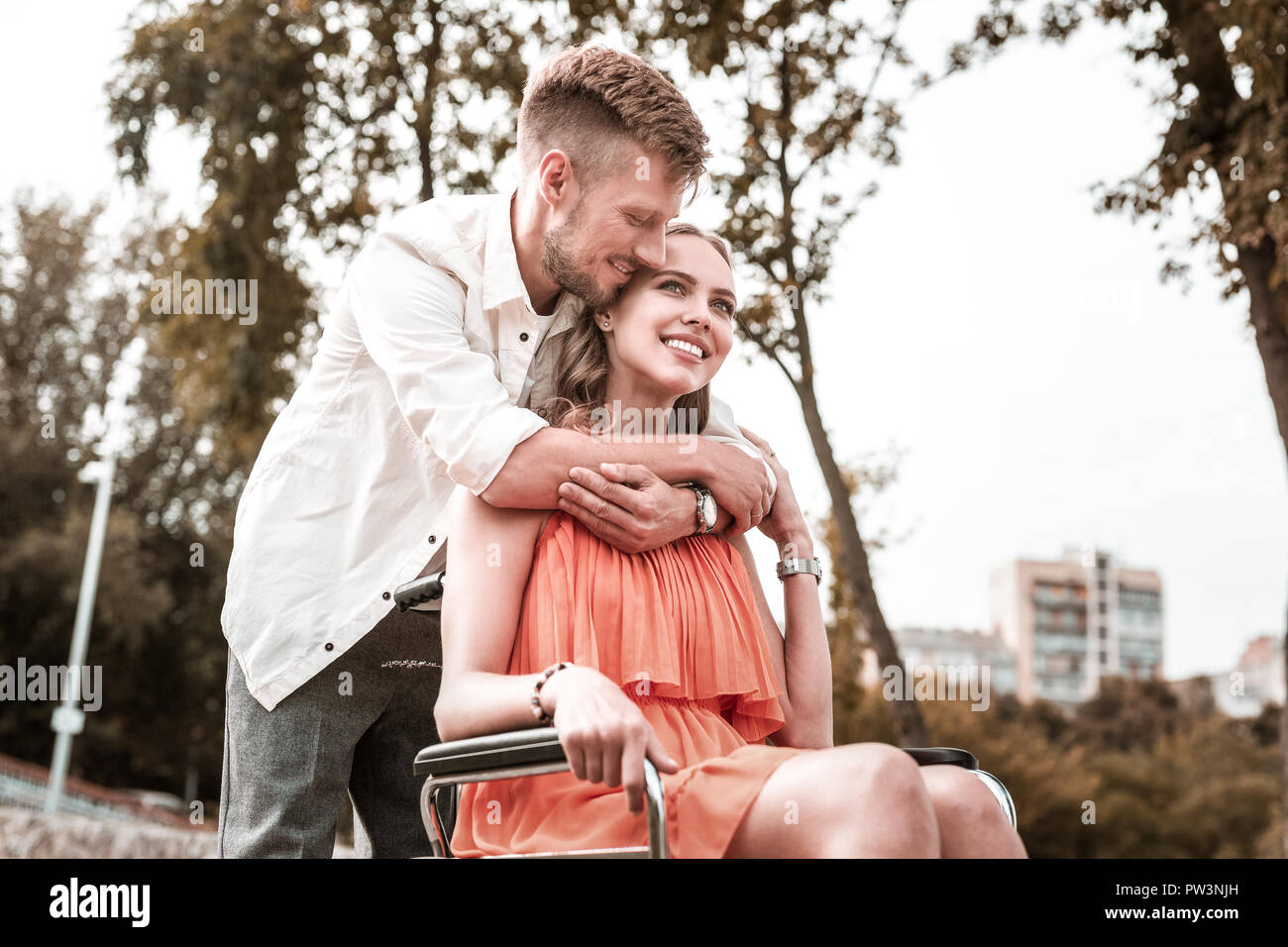 Calm man smiling and hugging girlfriend in wheelchair Stock Photo - Alamy