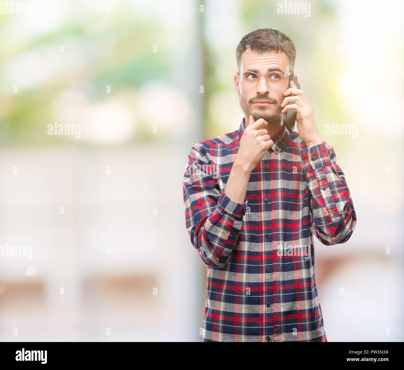 Young hipster adult man talking on the phone serious face thinking ...