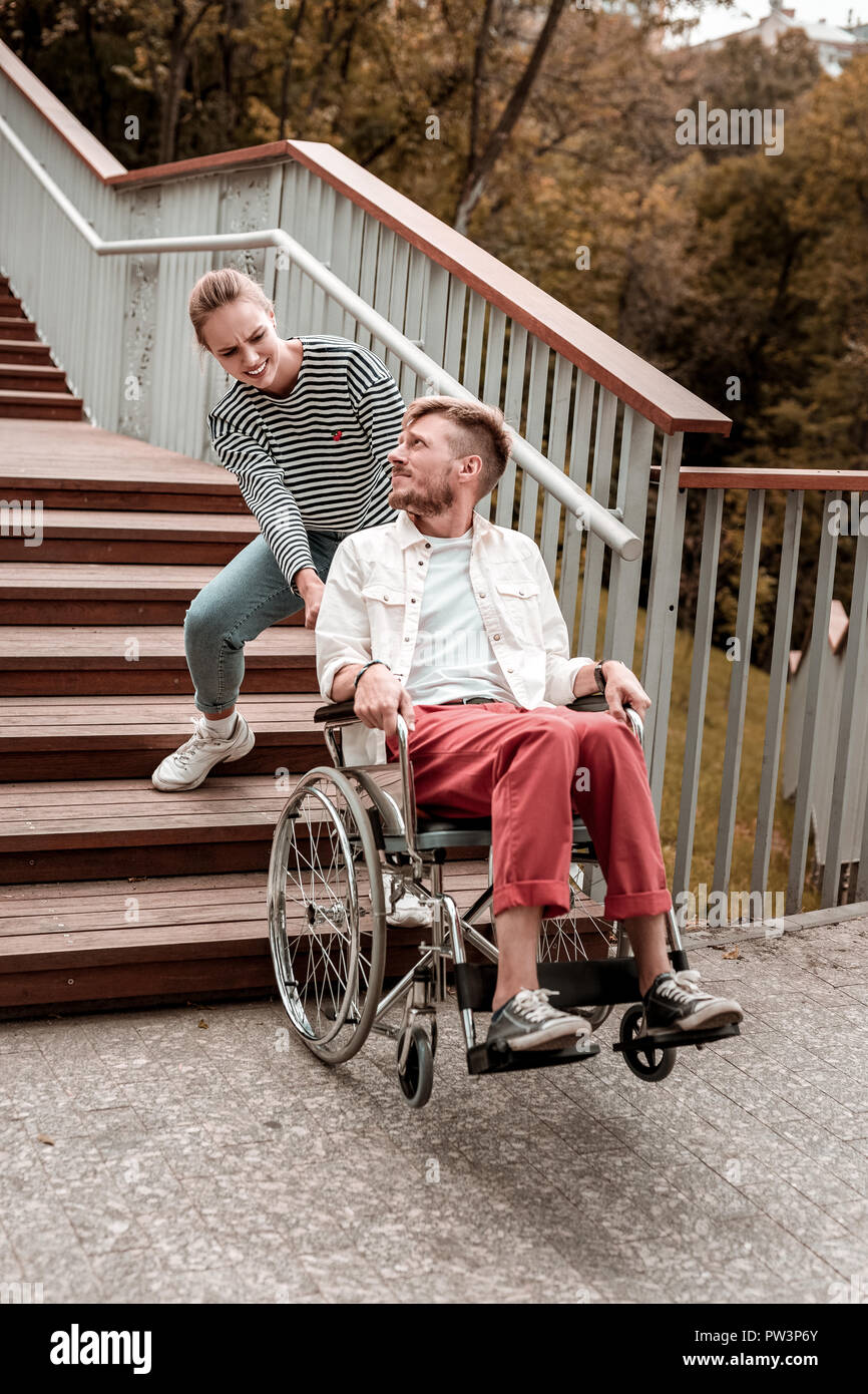 Sad invalid man looking at the tiny woman carrying his wheelchair Stock ...