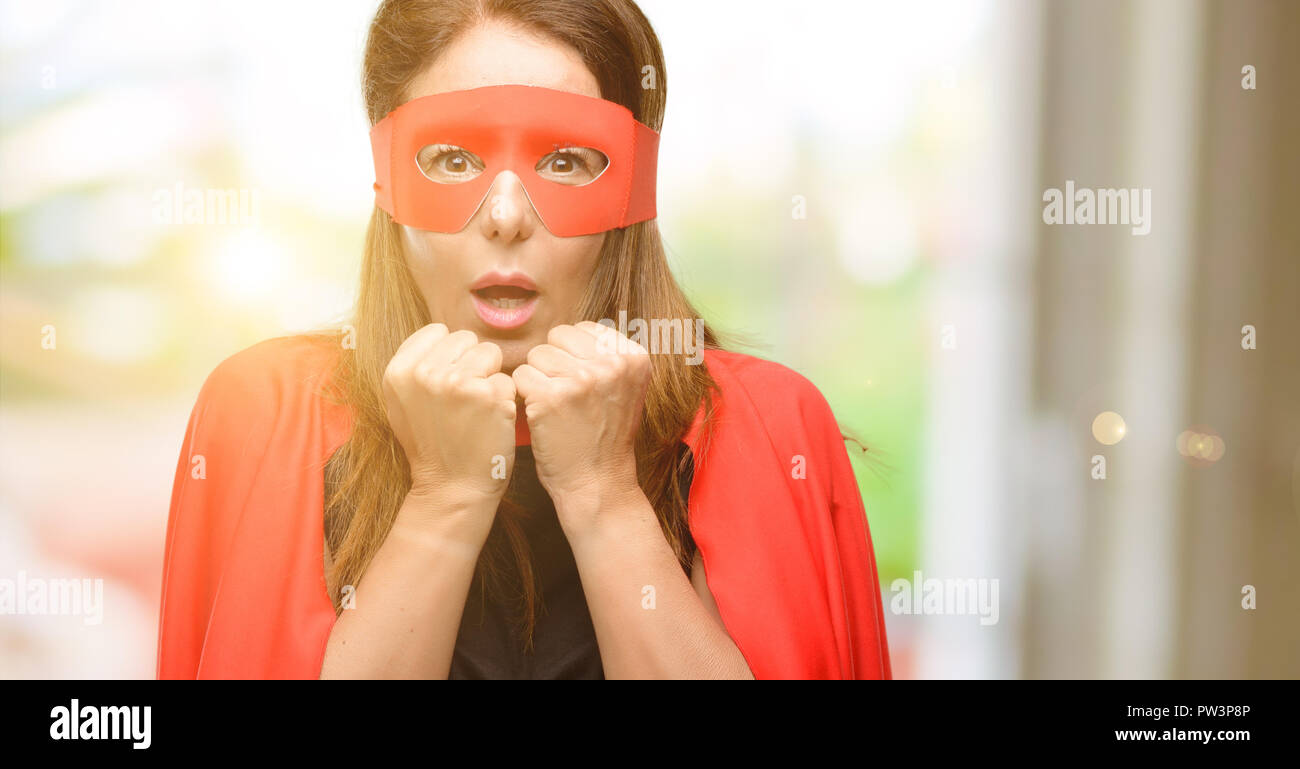 Middle age super hero woman wearing red mask and cape terrified and ...
