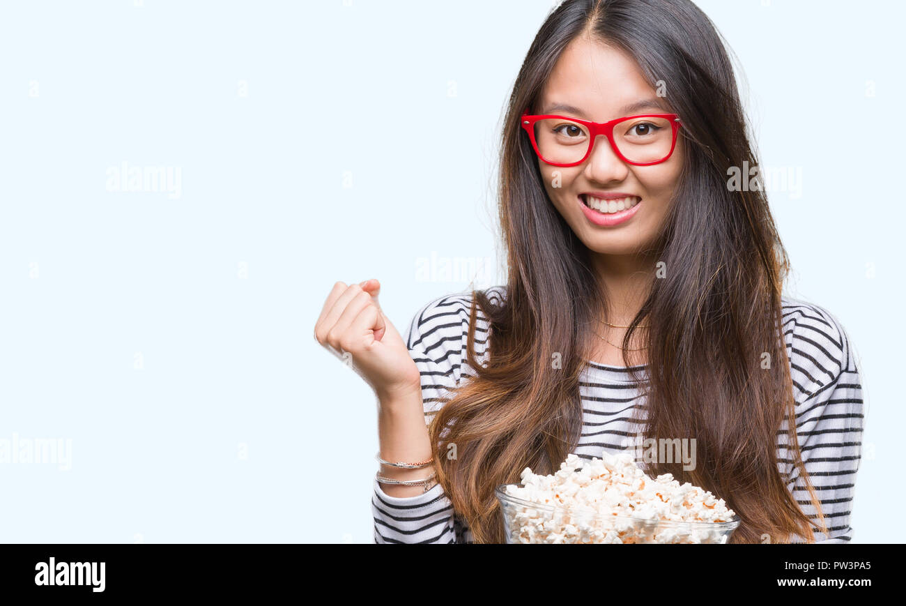 Young asian woman eating popcorn over isolated background screaming ...