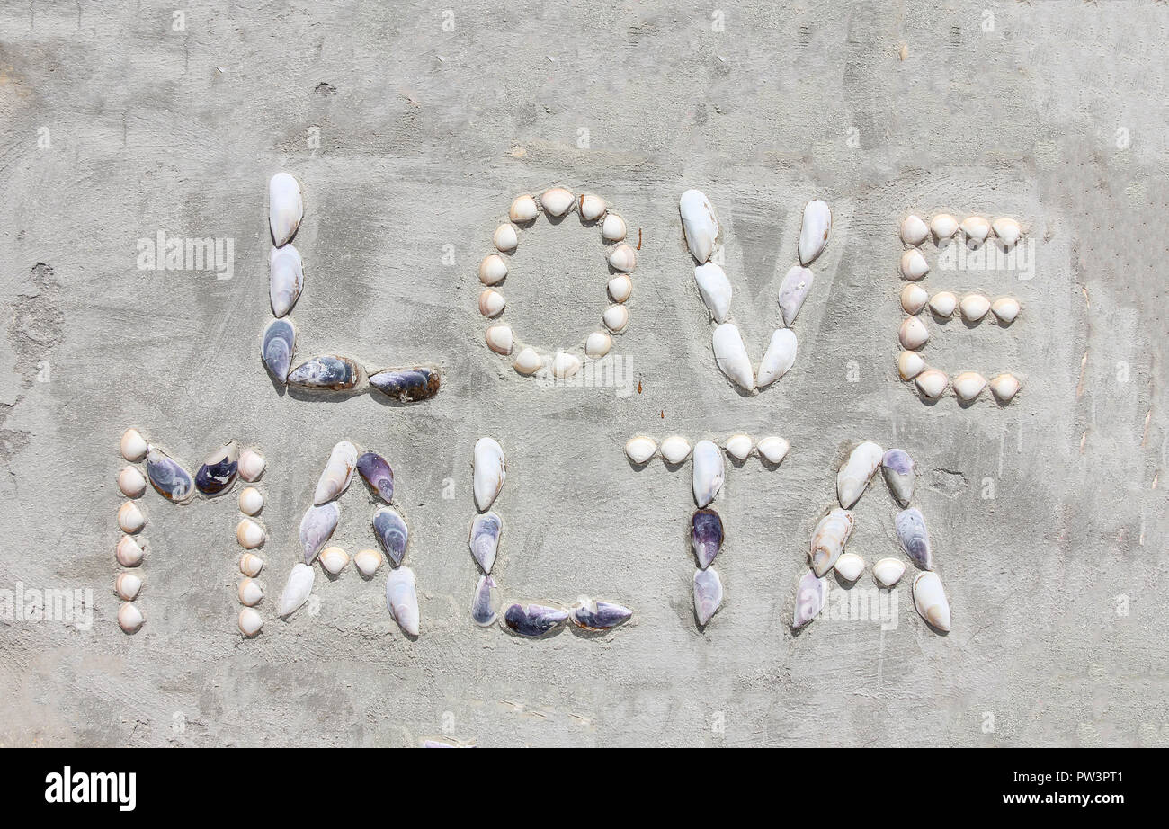 Shell letters make words Love Malta on cement wall background in sunny ...