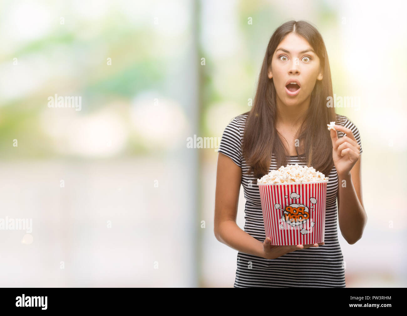 Young beautiful hispanic eating popcorn scared in shock with a surprise ...