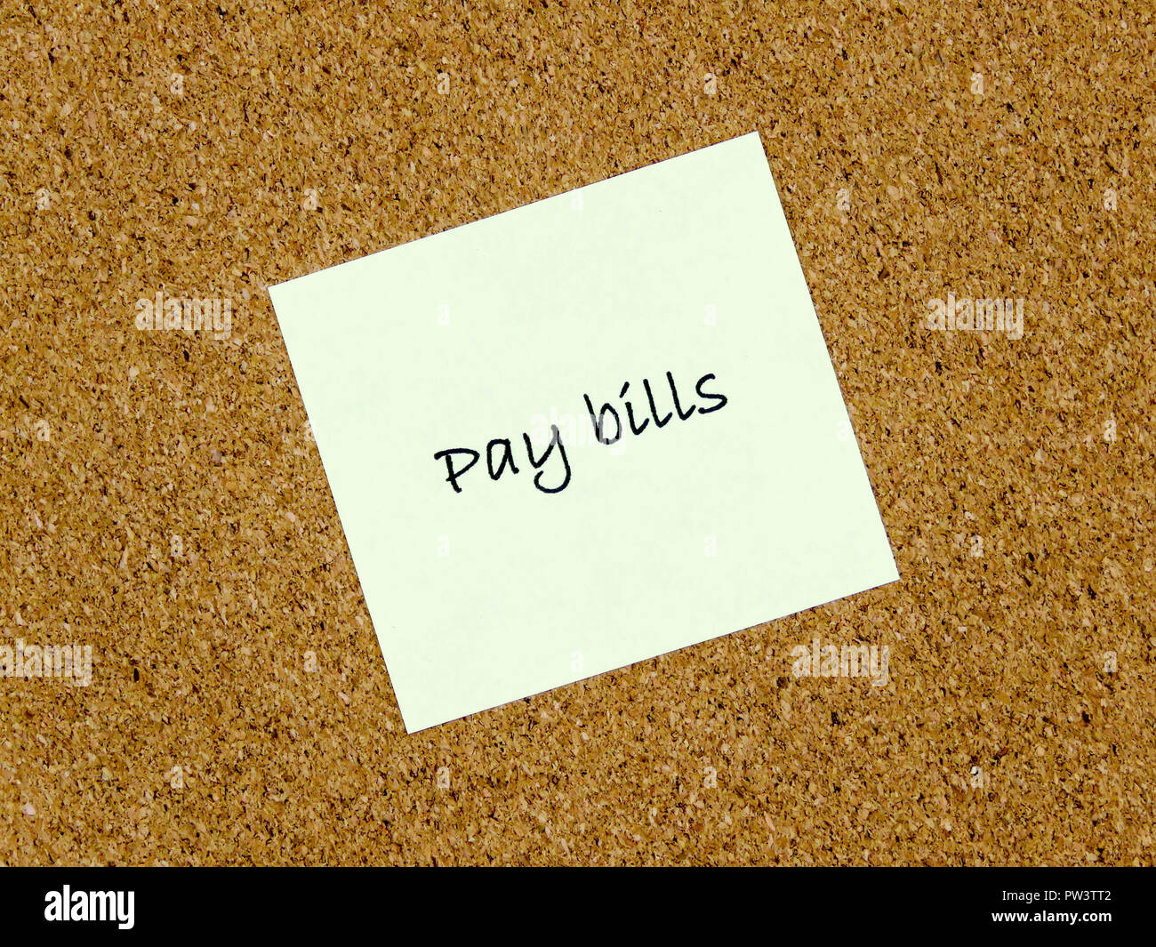 A yellow sticky note with pay bills written on it on a cork board ...