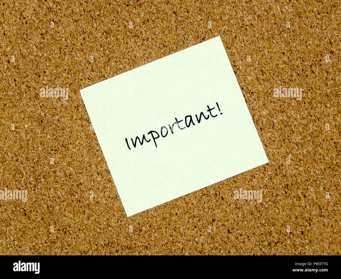 A yellow sticky note with important written on it on a cork board ...