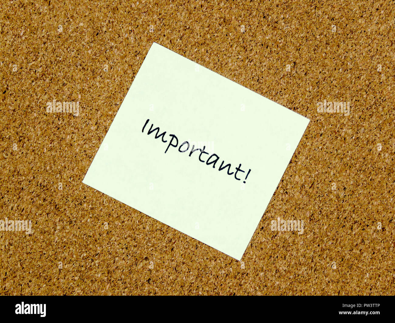 A yellow sticky note with important written on it on a cork board ...