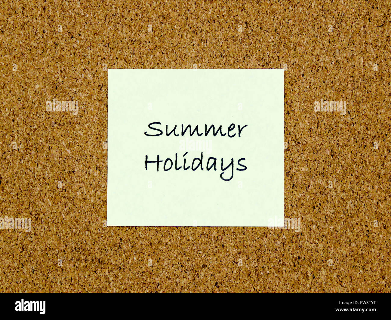 A yellow sticky note with summer holidays written on it on a cork board ...