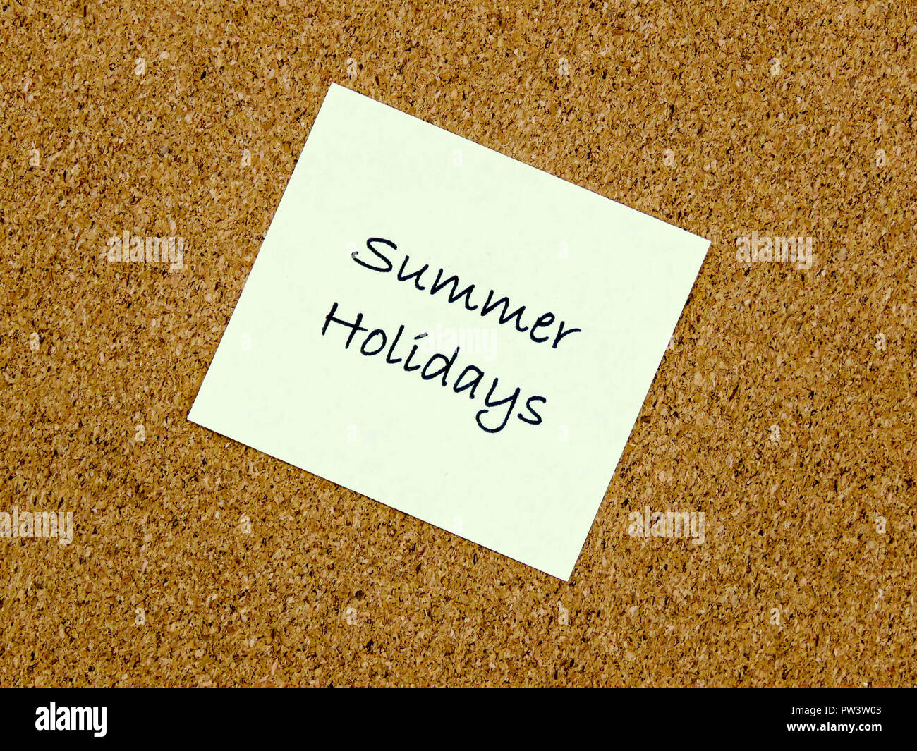 A yellow sticky note with summer holidays written on it on a cork board ...