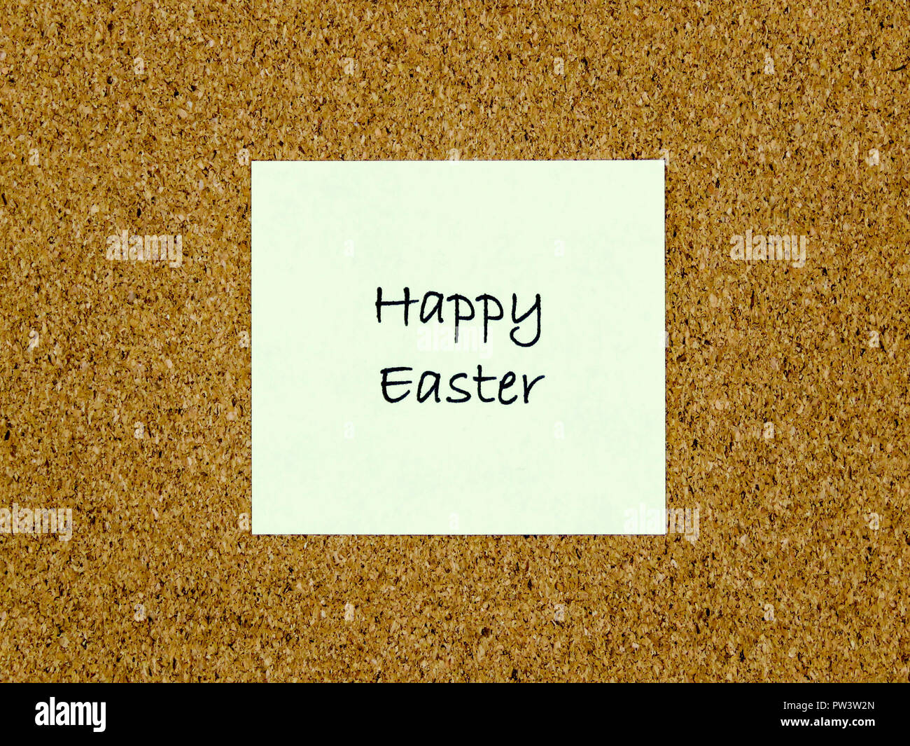 A yellow sticky note with happy easter written on it on a cork board ...