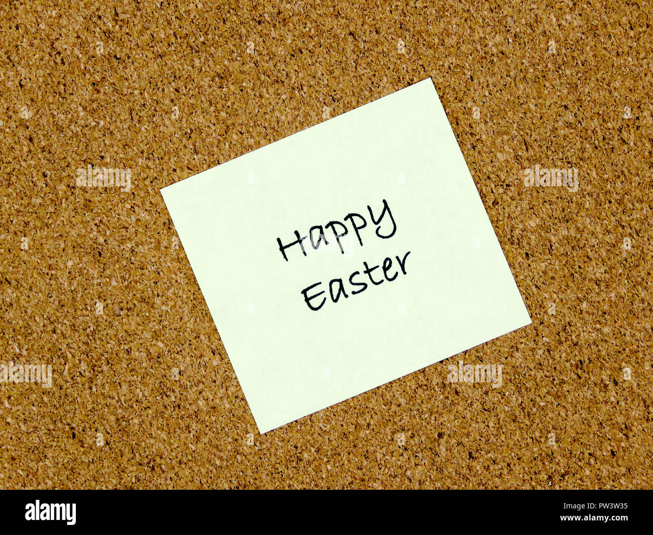 A yellow sticky note with happy easter written on it on a cork board ...