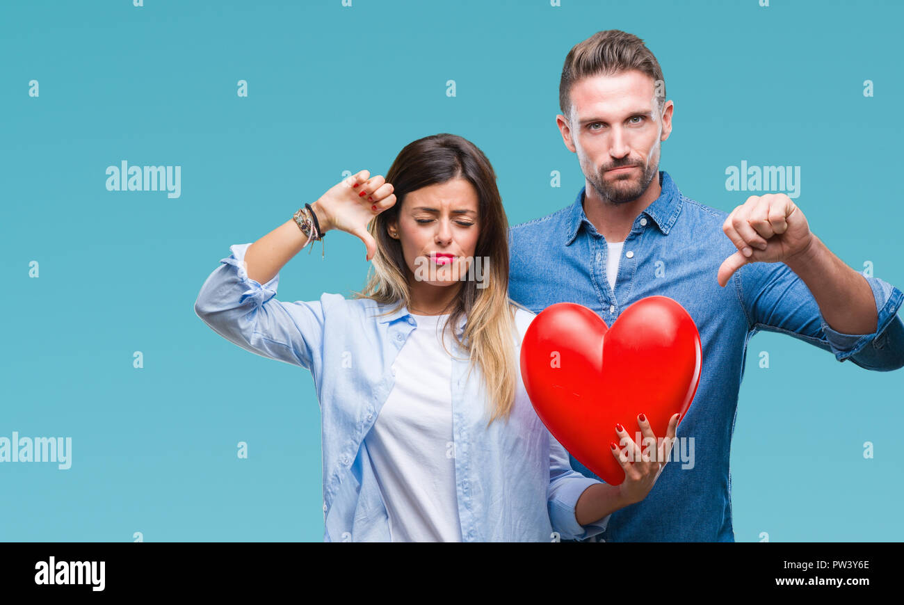 Young couple in love holding red heart over isolated background with ...