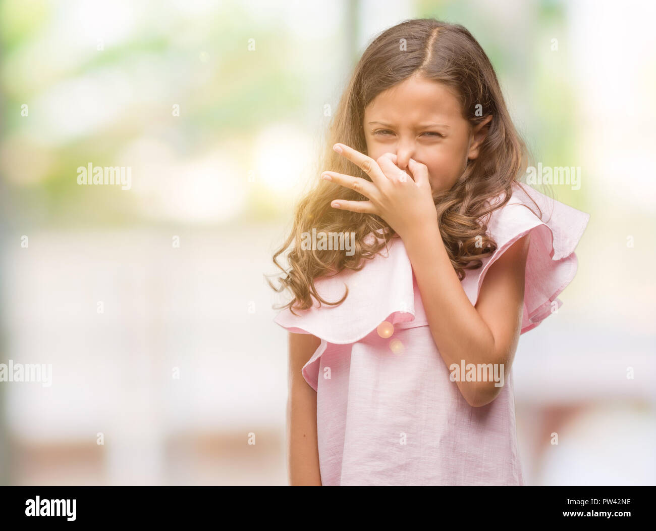 Brunette hispanic girl wearing pink dress smelling something stinky and ...