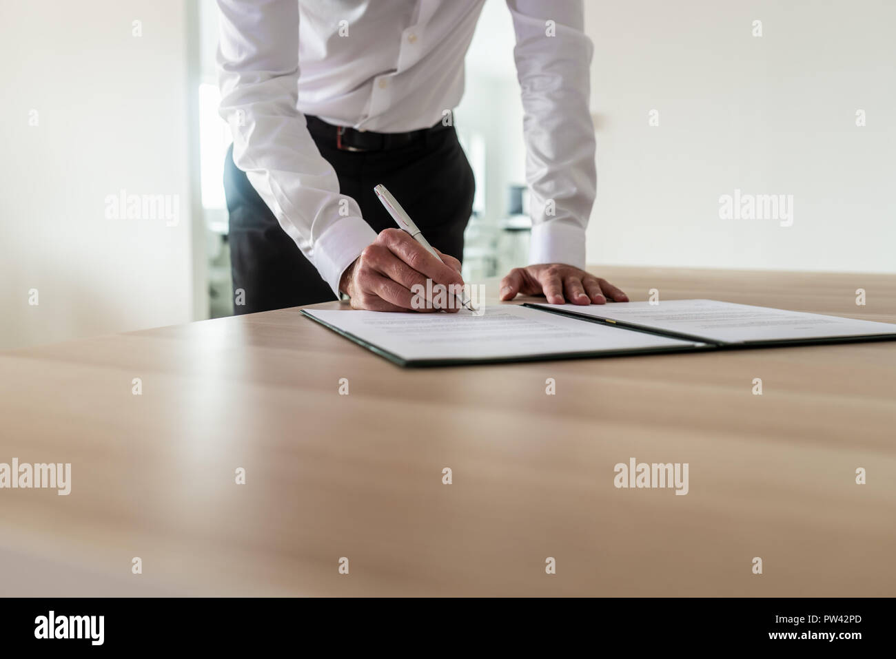 Entrepreneur standing behind office desk leaning to sign legal document ...