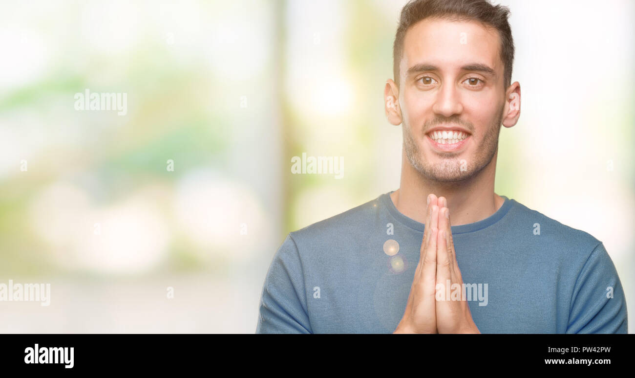 Handsome young casual man praying with hands together asking for ...