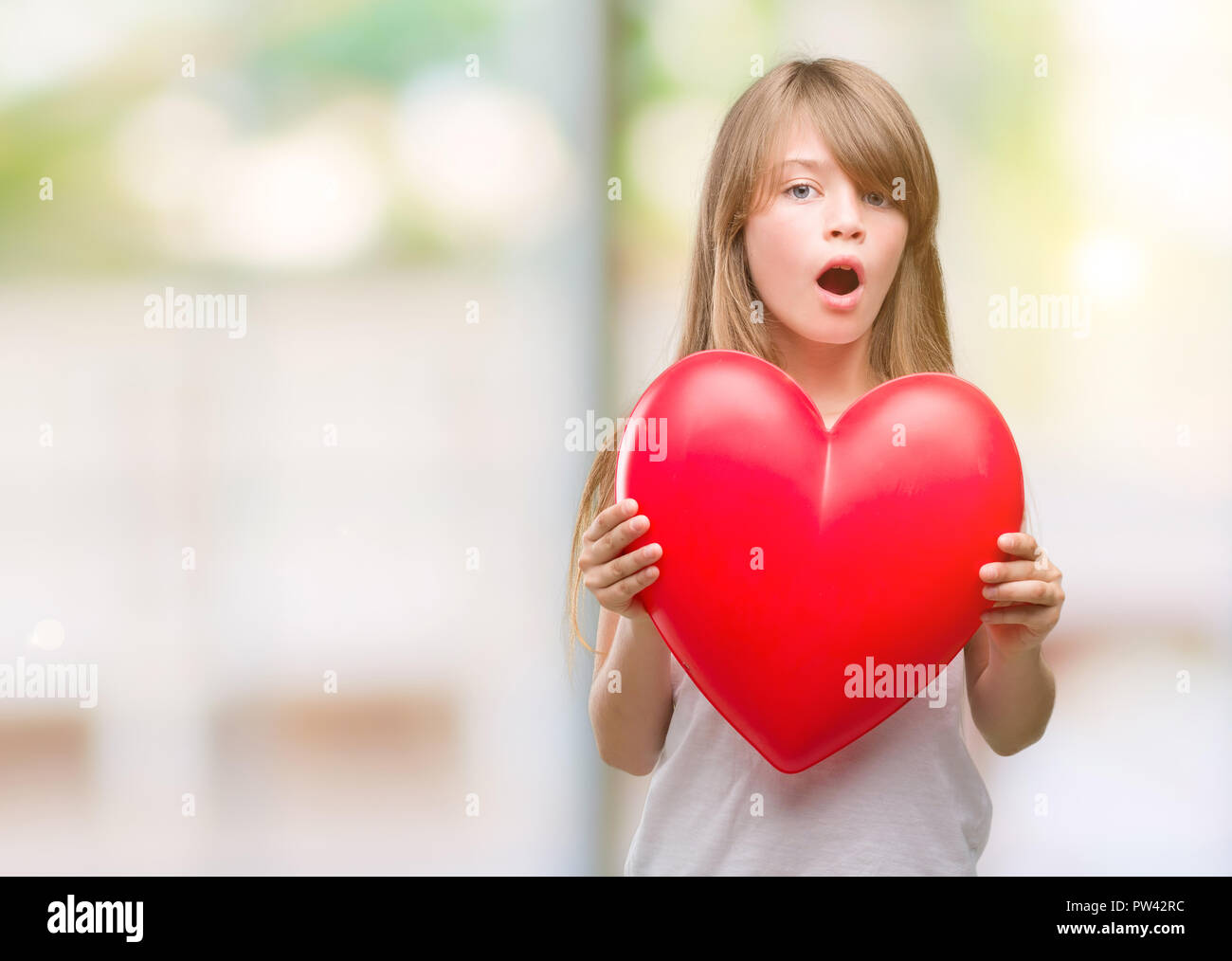 Young blonde toddler holding a red heart scared in shock with a ...
