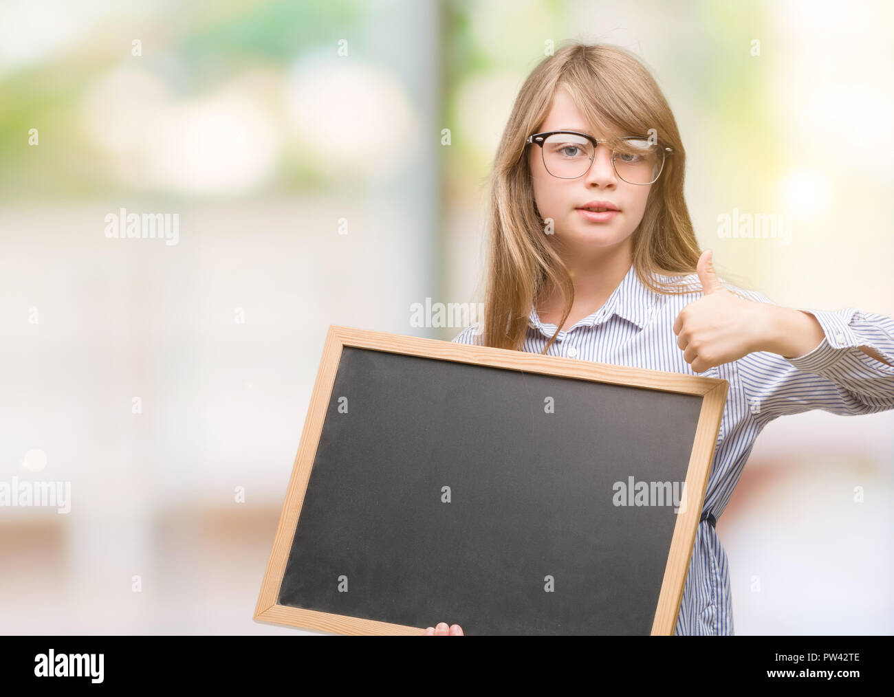 Young blonde child holding blackboard happy with big smile doing ok ...