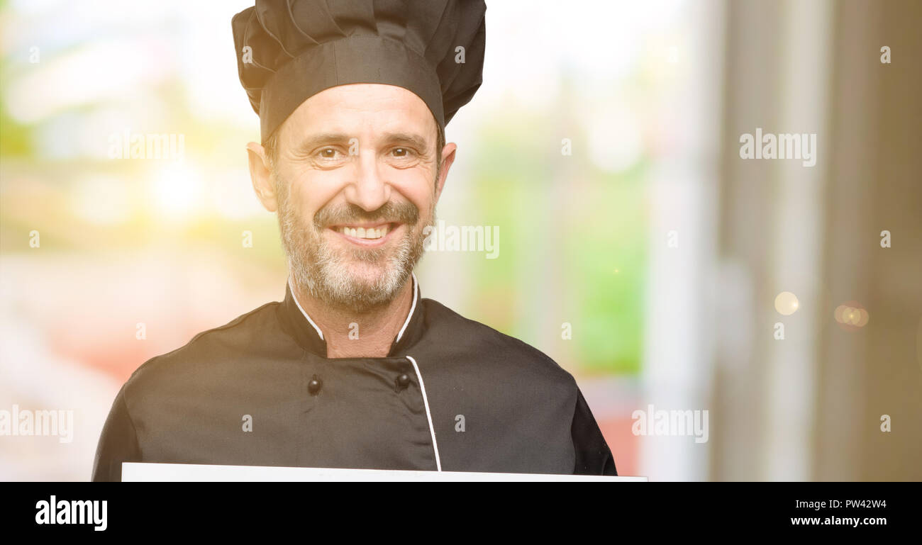 Senior cook man, wearing chef hat holding blank advertising banner ...