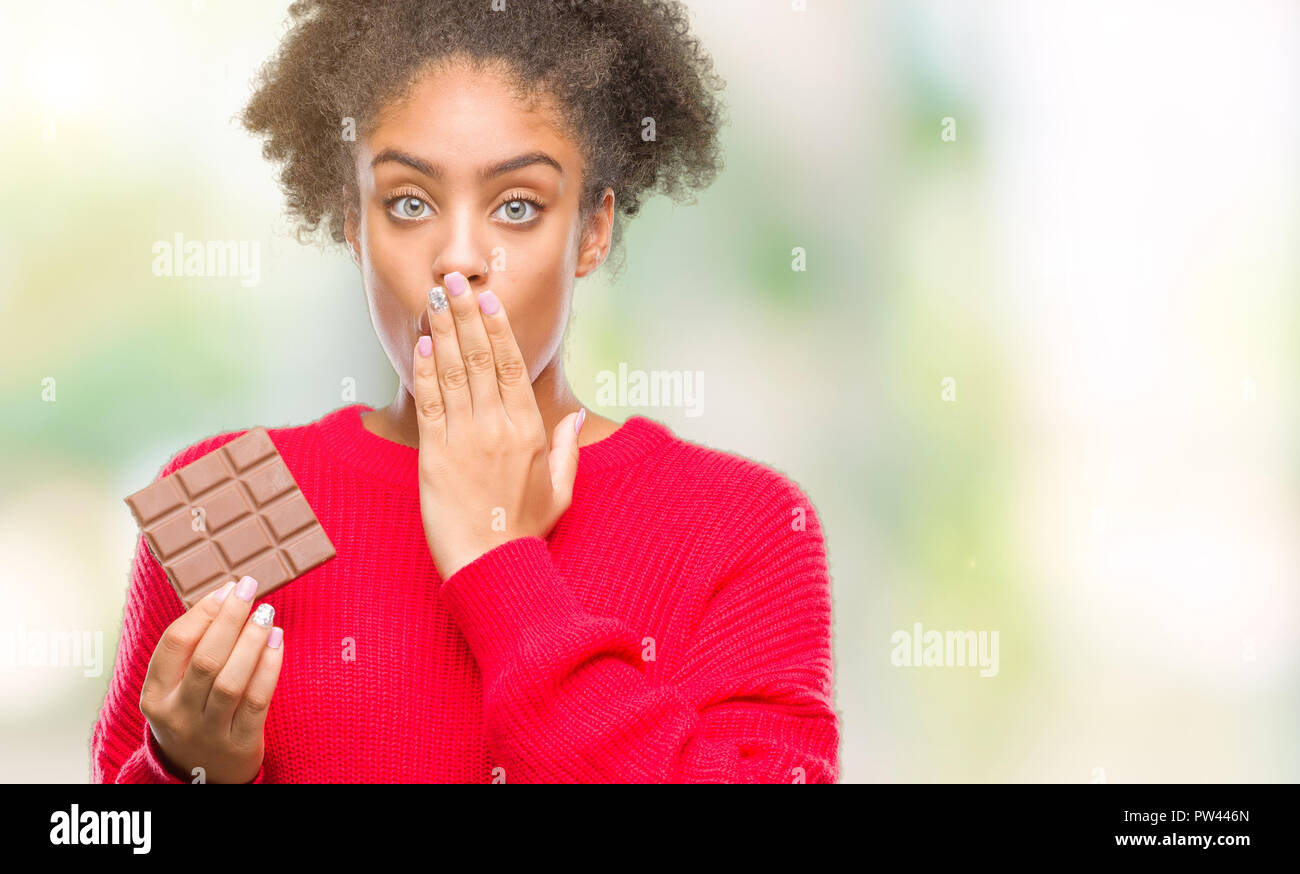 Young afro american woman eating chocolate bar over isolated background ...