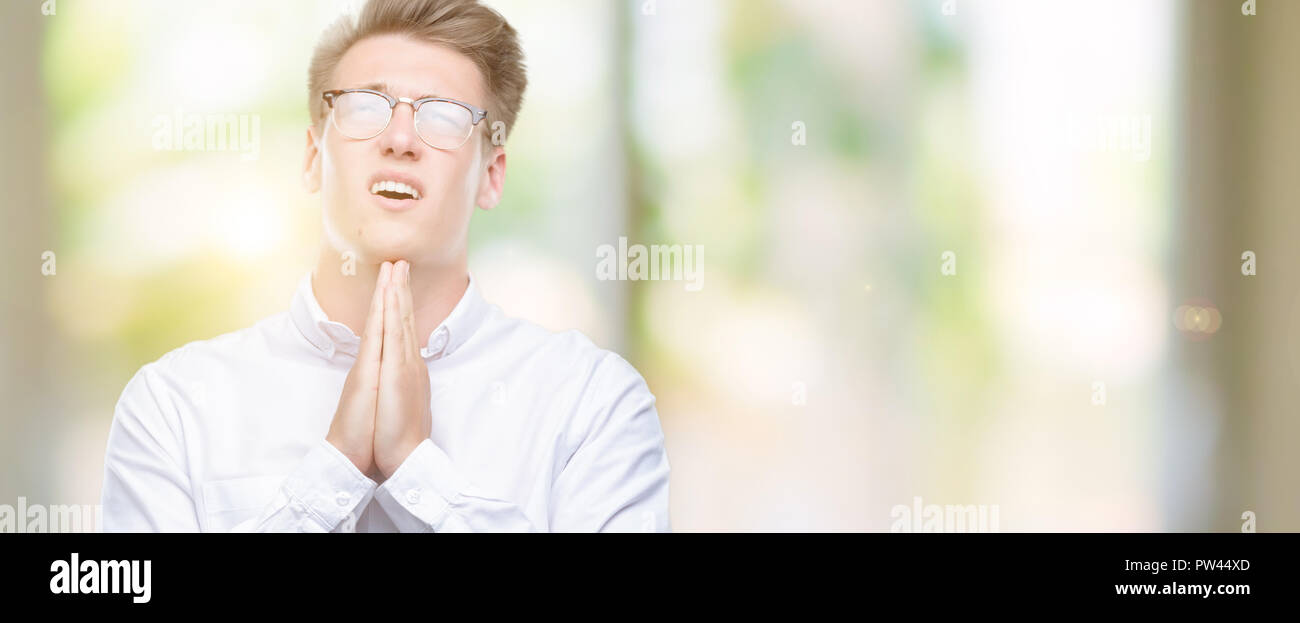 Young handsome blond man begging and praying with hands together with ...