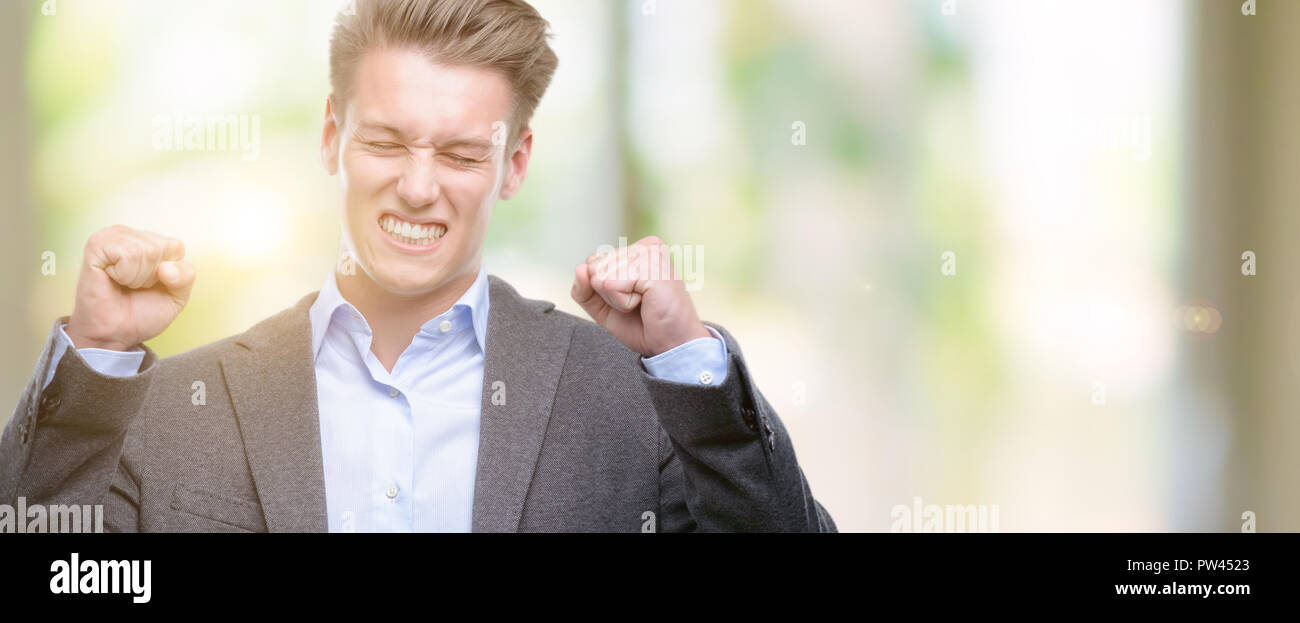 Young handsome blond business man excited for success with arms raised ...