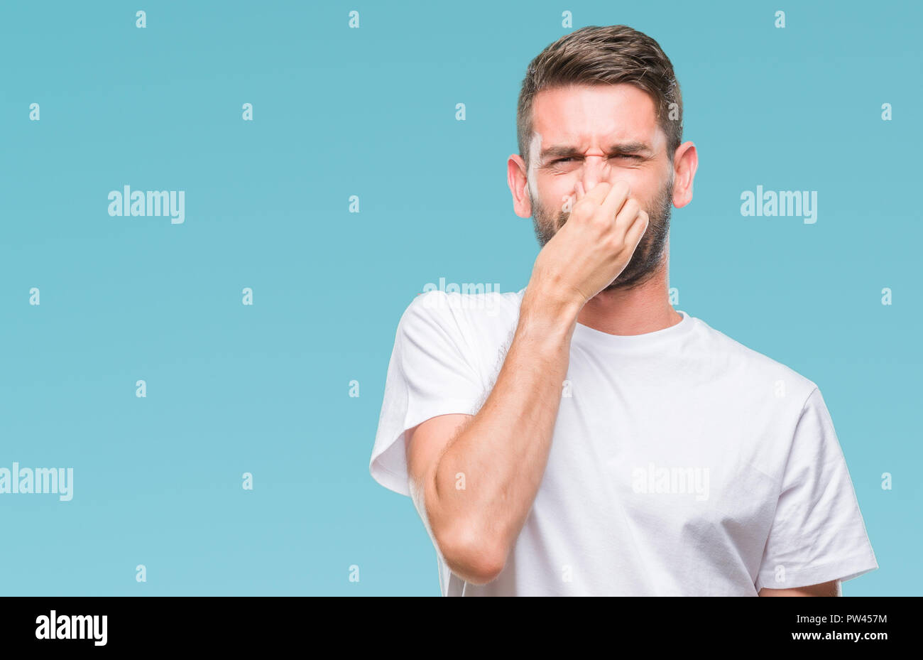 Young handsome man over isolated background smelling something stinky ...
