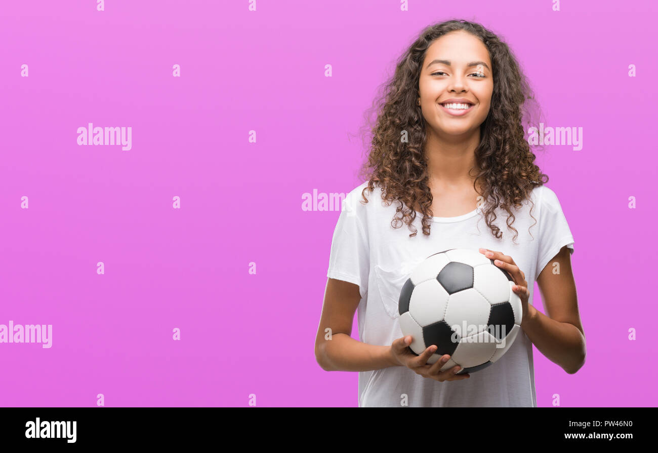 Young hispanic woman holding soccer football ball with a happy face ...