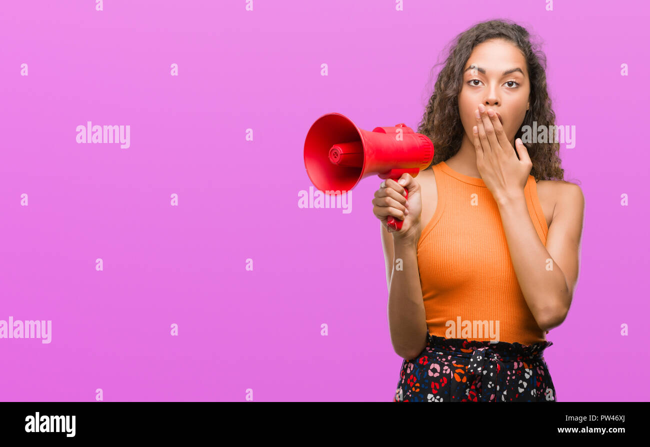 Young hispanic woman holding megaphone cover mouth with hand shocked ...