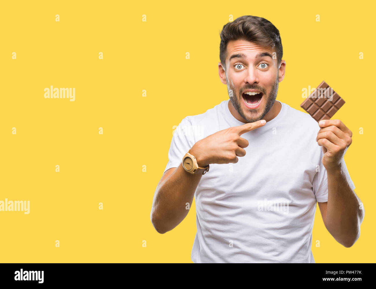 Young handsome man eating chocolate bar over isolated background very ...