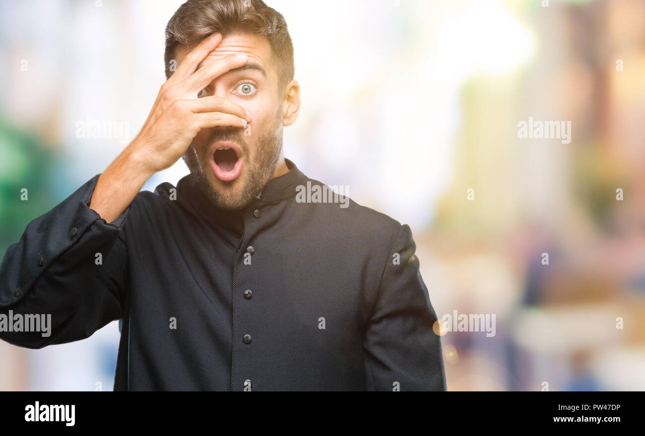 Young catholic christian priest man over isolated background peeking in ...