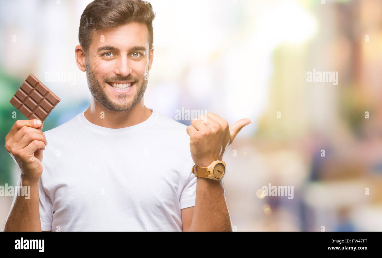 Young handsome man eating chocolate bar over isolated background ...