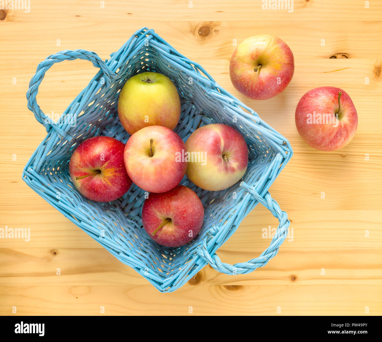 Red apples in blue wooden basket on wooden table. Two apples are ...