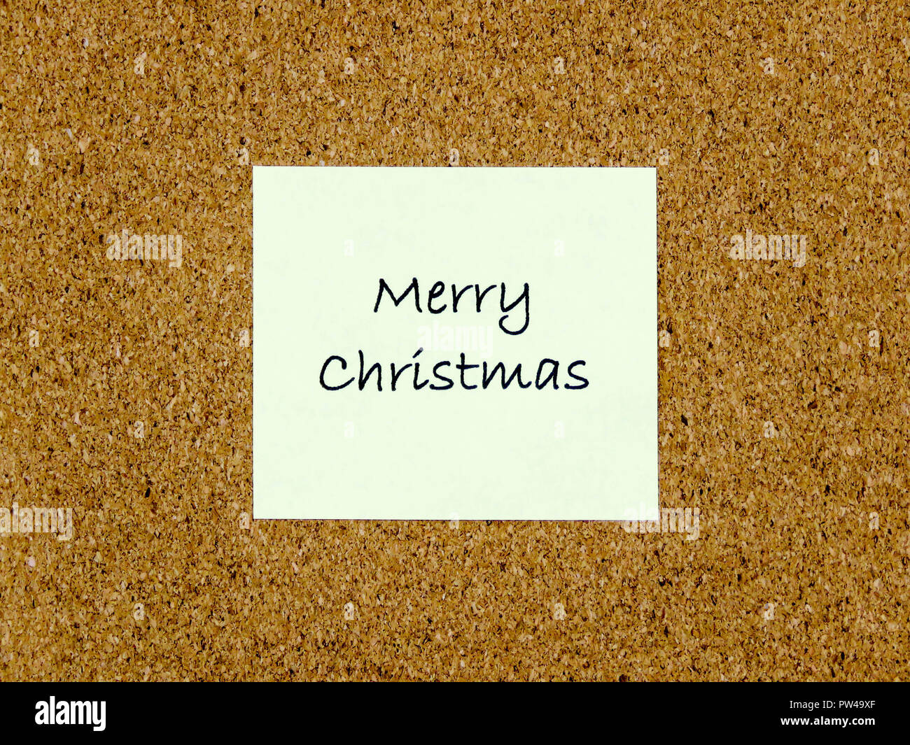 A yellow sticky note with Merry Christmas written on it on a cork board ...