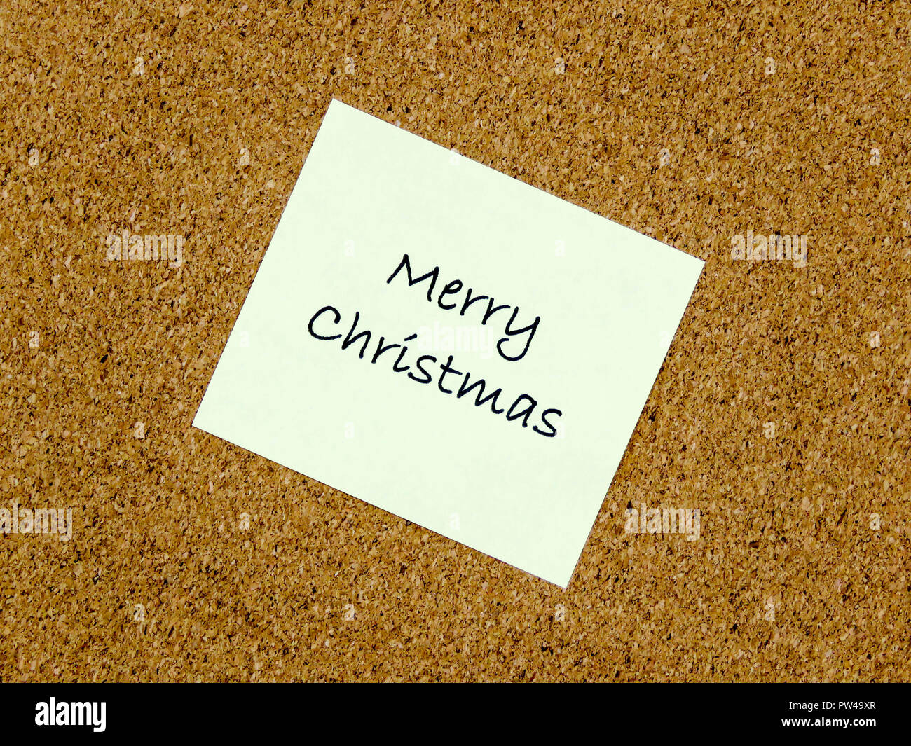 A yellow sticky note with Merry Christmas written on it on a cork board ...