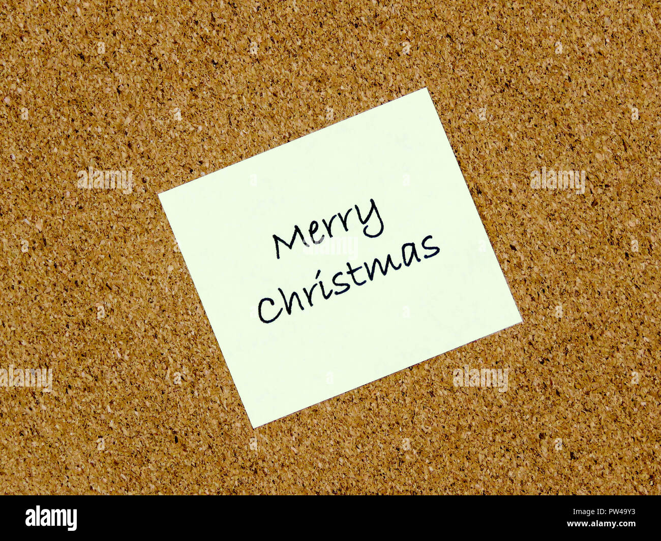 A yellow sticky note with Merry Christmas written on it on a cork board ...