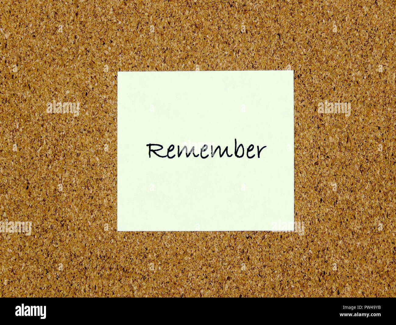 A yellow sticky note with remember written on it on a cork board ...