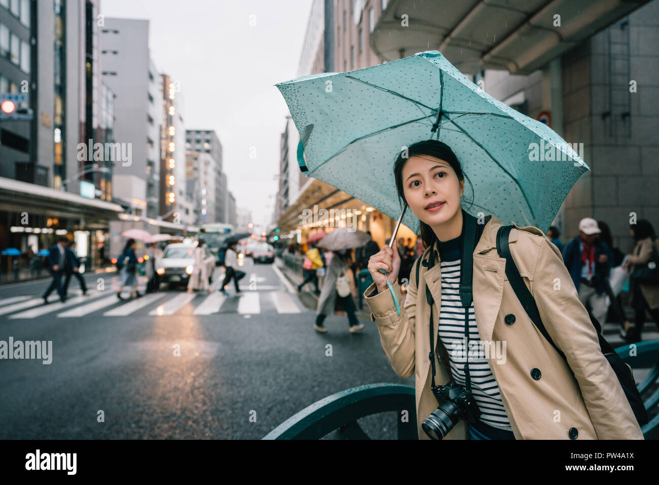 beautiful woman standing on the busy street, holding blue umbrella in ...