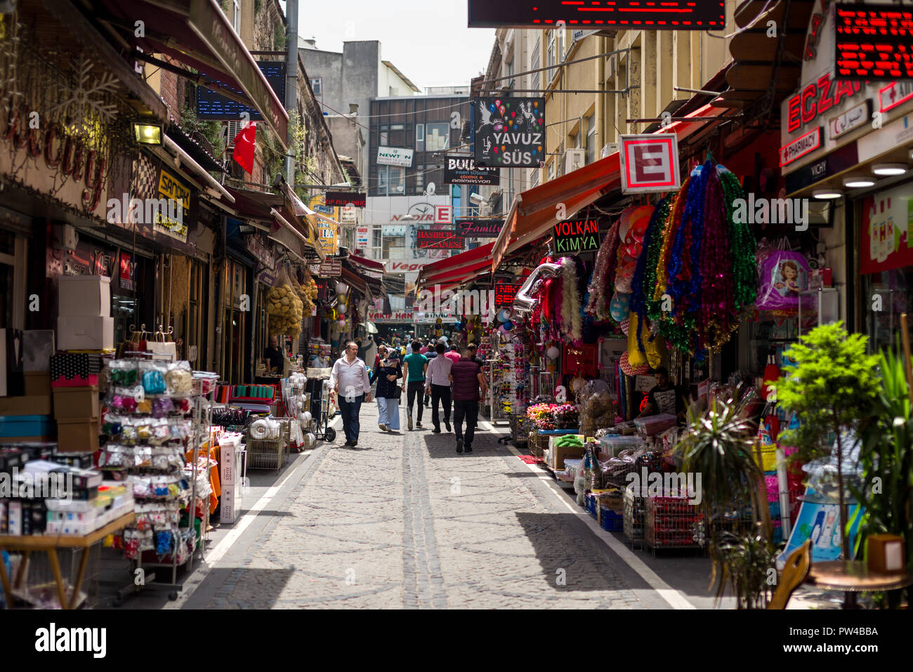 People walking down a cobbled street past small shops with goods on ...