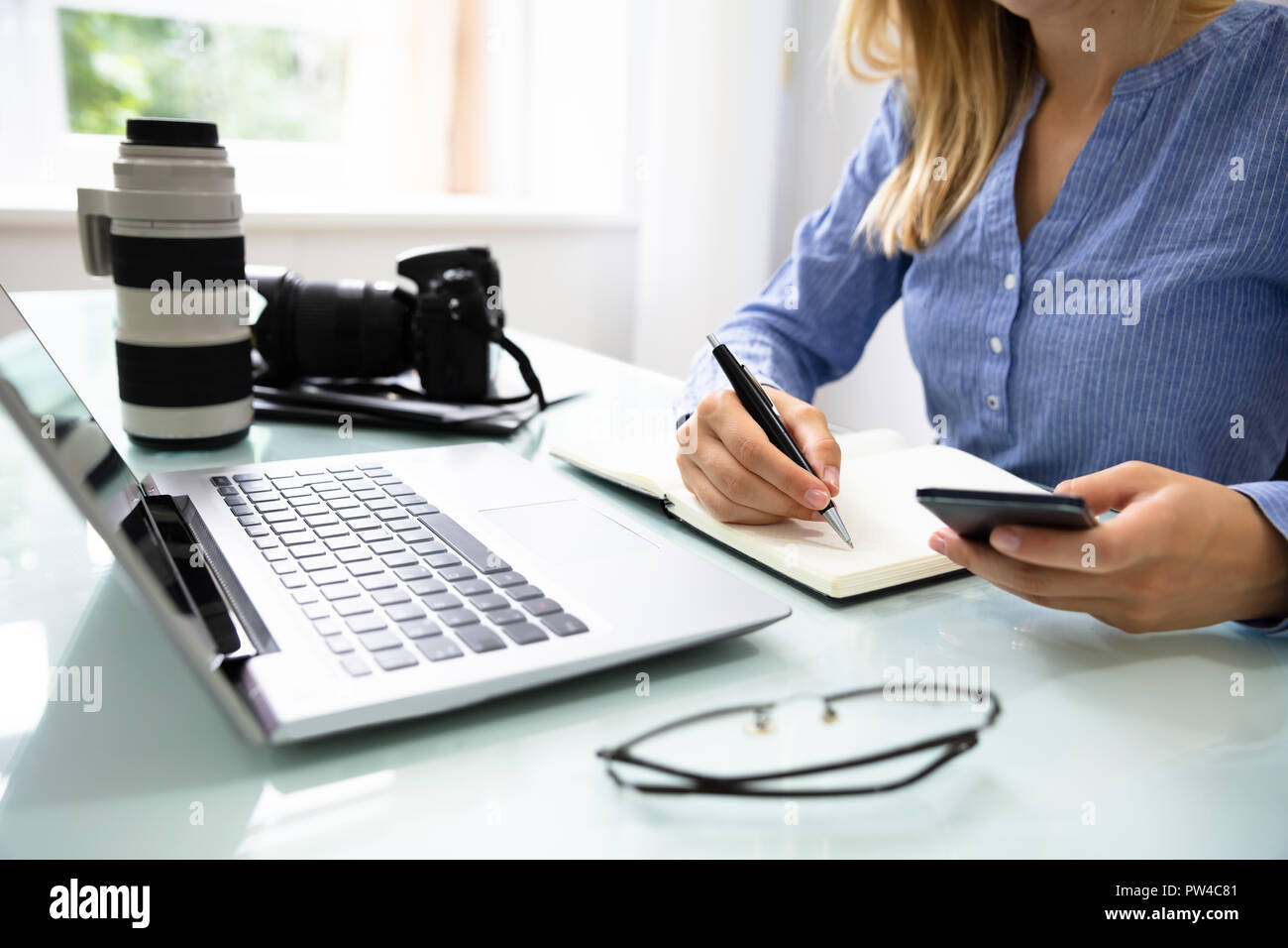 Female Editor Writing Notes In Diary With Laptop And DSLR Camera On ...