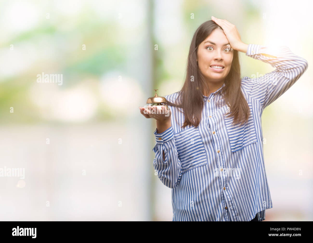 Young beautiful hispanic holding hotel ring bell stressed with hand on ...
